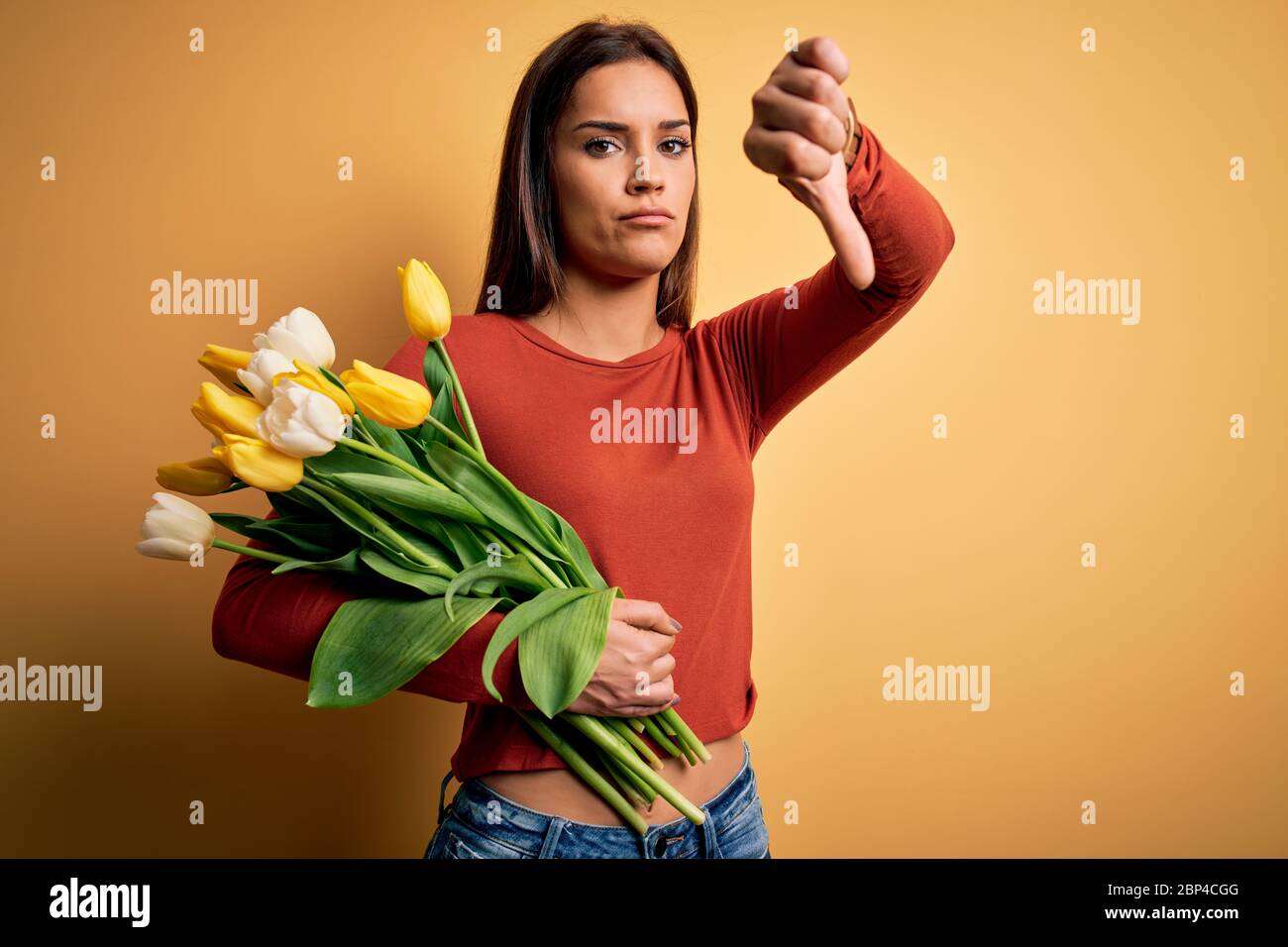 Young beautiful brunette woman holding bouquet of tulips flowers over ...