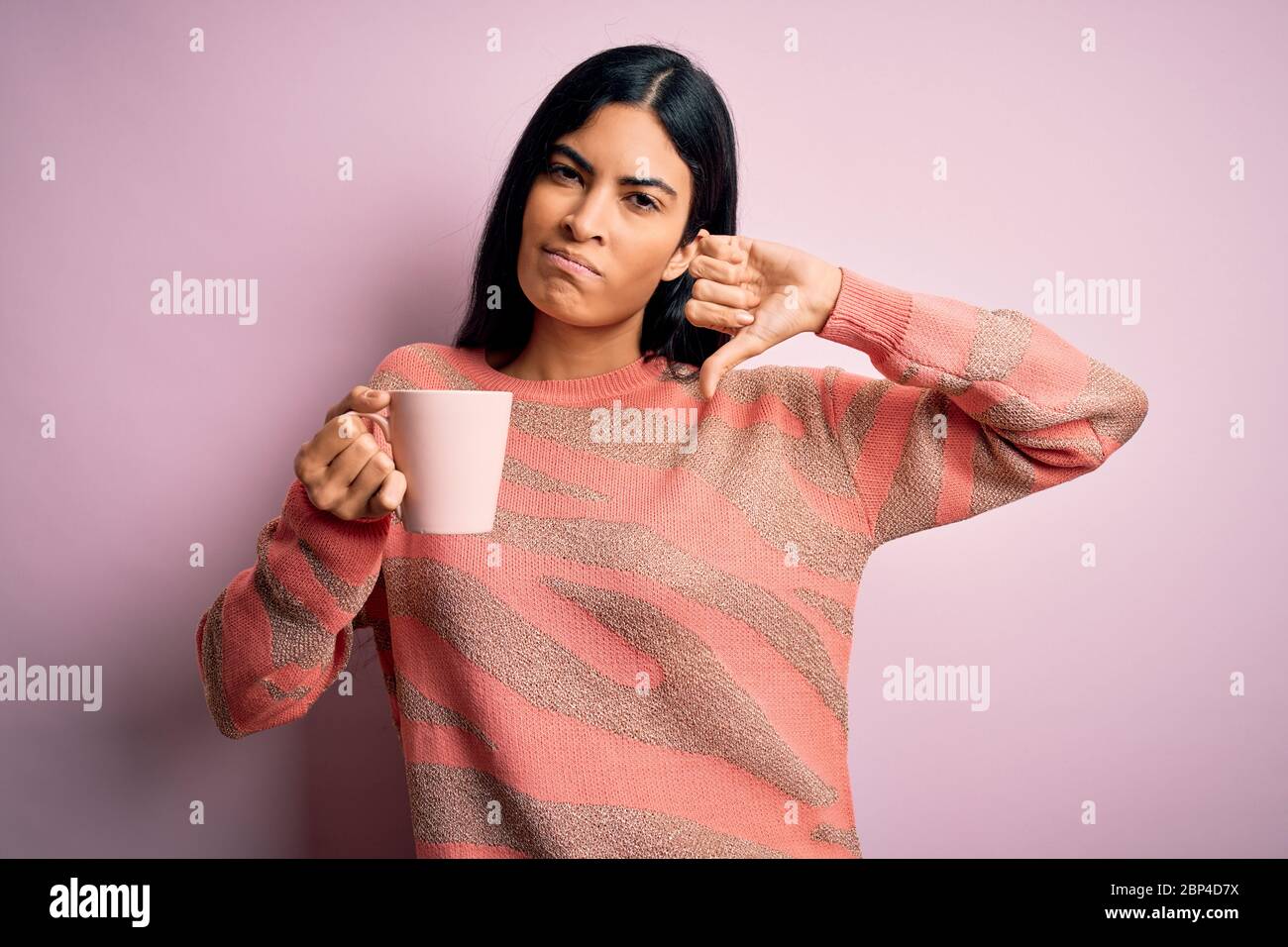 Young beautiful hispanic woman drinking a cup of hot coffee over pink isolated background with ...