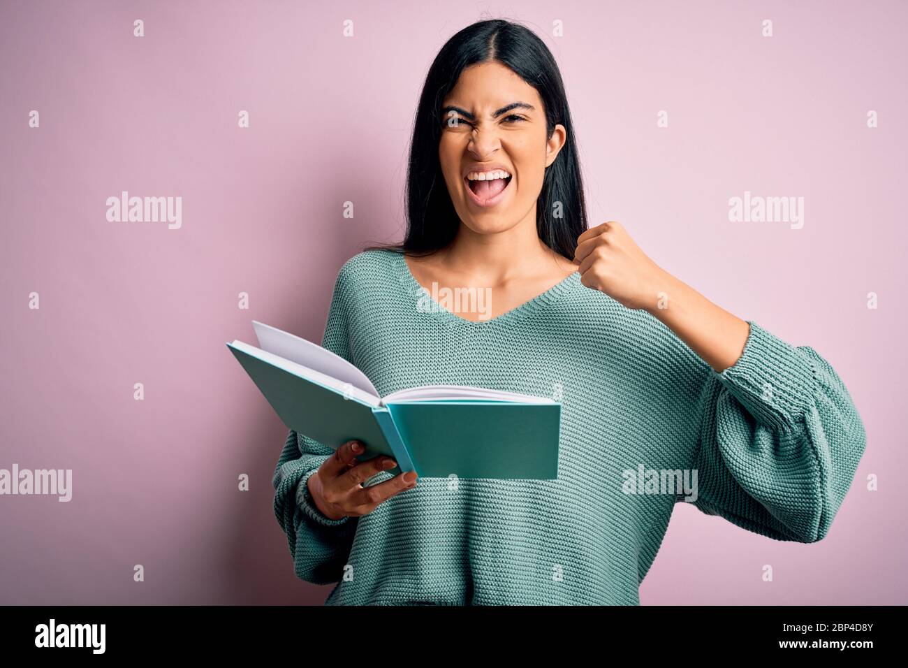Young beautiful hispanic student woman reading a book over pink ...
