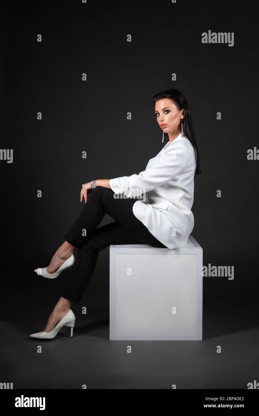 beautiful girl sitting sideways with cross legs on a white cube against ...