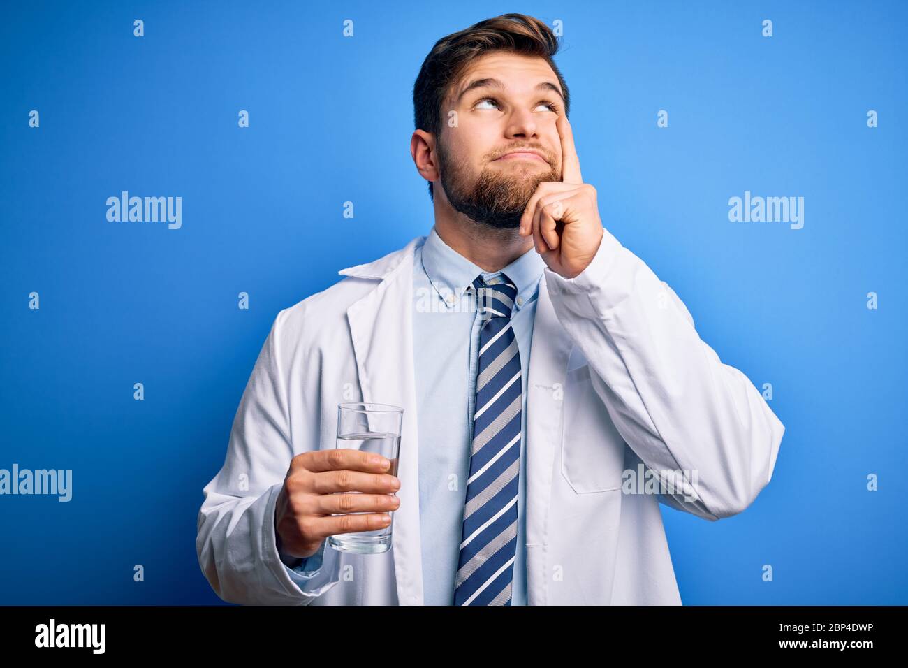 Young blond doctor man with beard and blue eyes wearing coat and tie ...