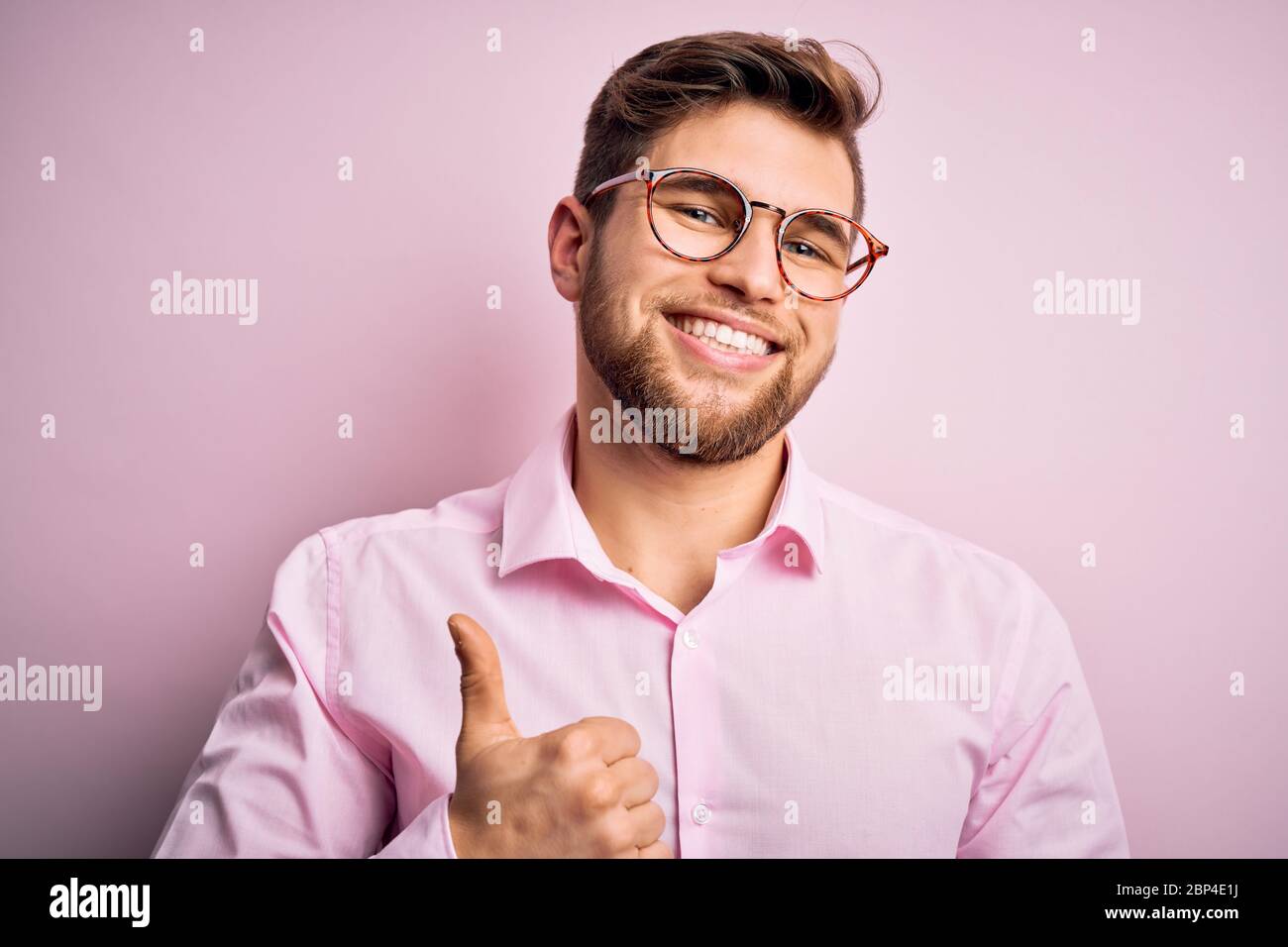 Young handsome blond man with beard and blue eyes wearing pink shirt ...