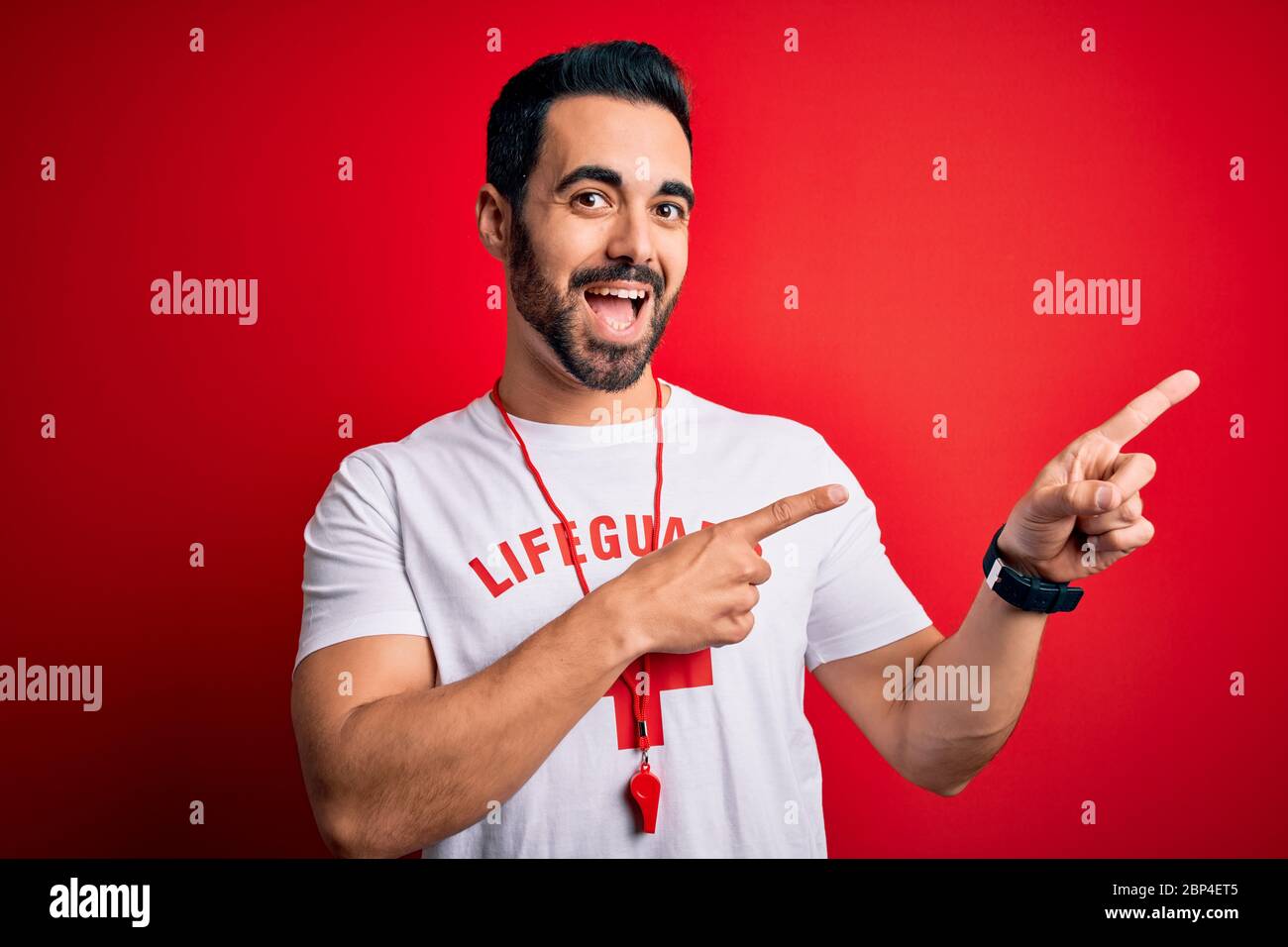 Young handsome lifeguard man with beard wearing whistle over isolated ...