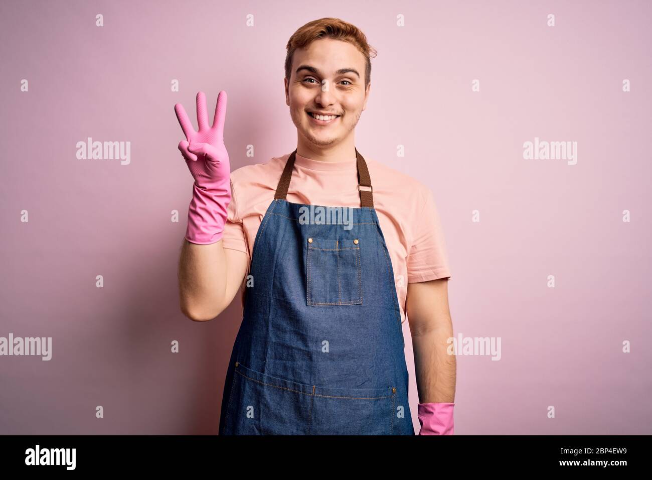 Young Handsome Redhead Cleaner Man Doing Housework Wearing Apron And Gloves Showing And Pointing