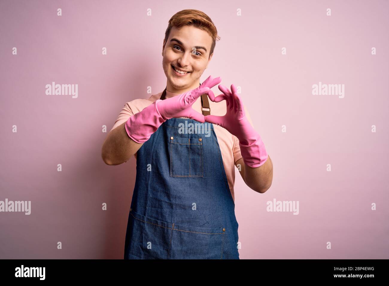 Young Handsome Redhead Cleaner Man Doing Housework Wearing Apron And Gloves Smiling In Love