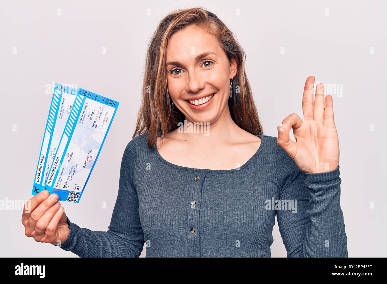 Young beautiful blonde woman holding boarding pass doing ok sign with ...