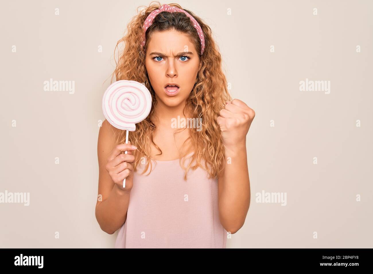 Young beautiful blonde woman with blue eyes eating sweet candy lollipop ...