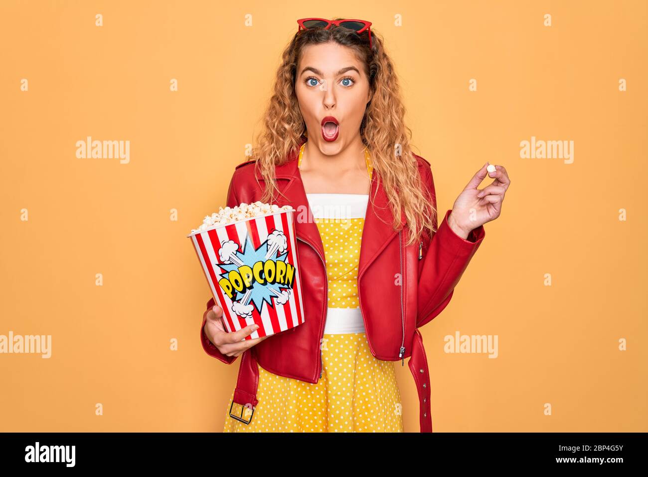 Beautiful blonde woman with blue eyes eating salty popcorn snack over ...