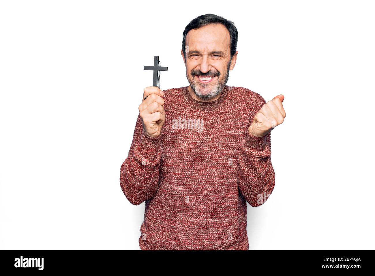 Middle age handsome catholic man praying holding christian cross over ...