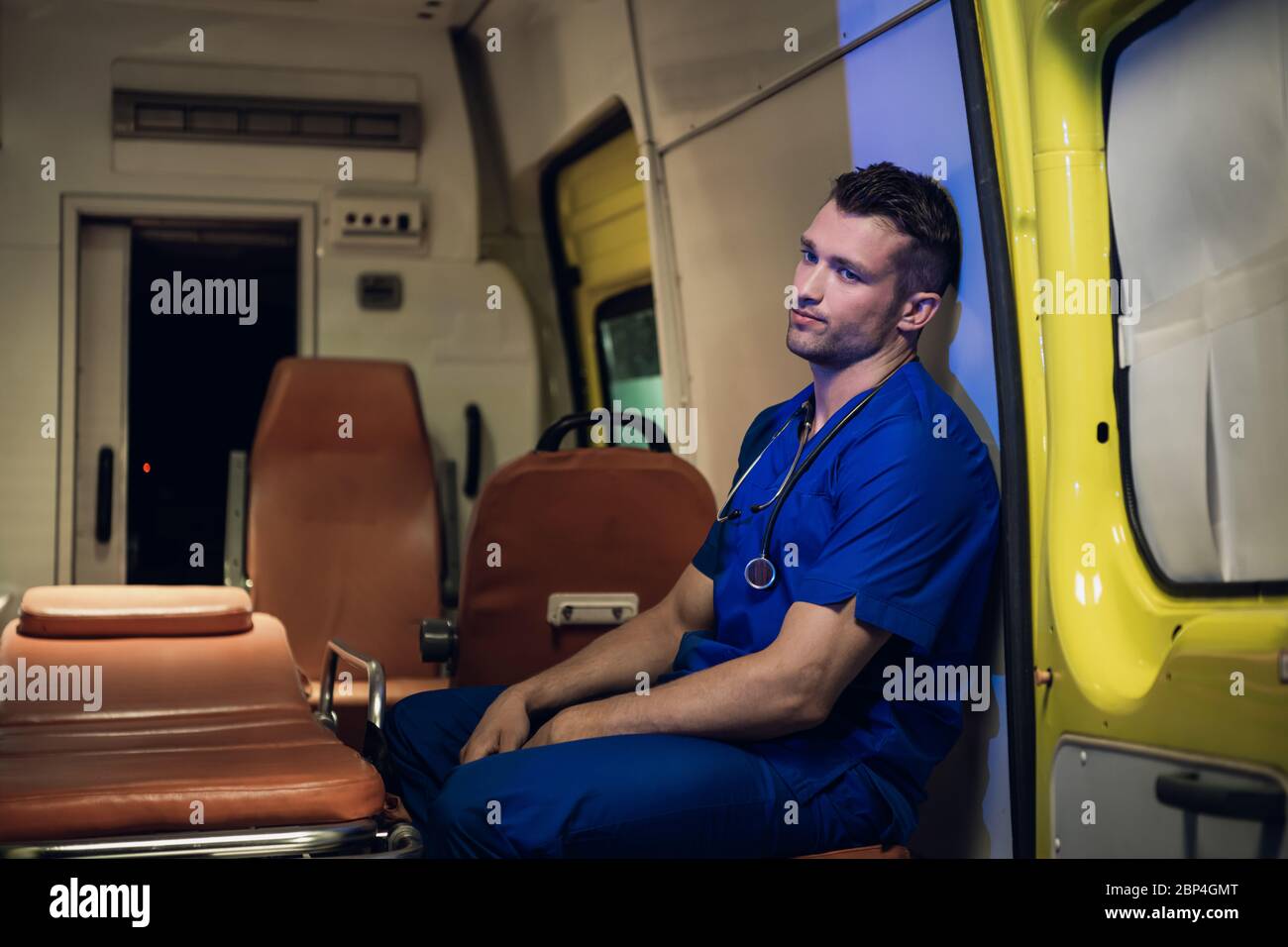 Overworked paramedic in a blue uniform sitting in an ambulance car ...