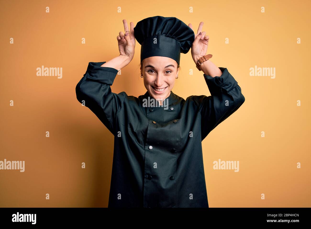 Young beautiful chef woman wearing cooker uniform and hat standing over ...