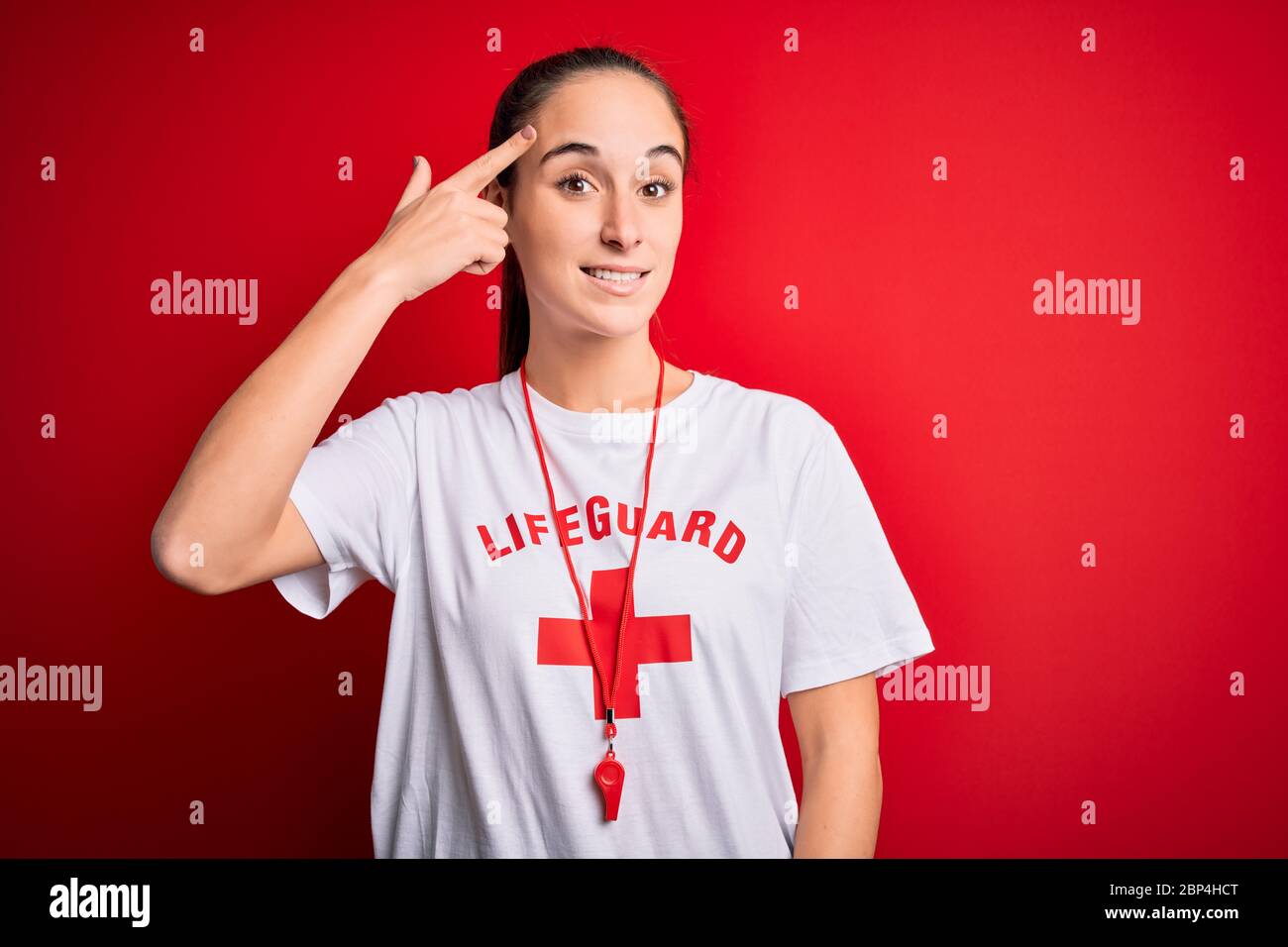 Beautiful lifeguard woman wearing t-shirt with red cross using whistle ...