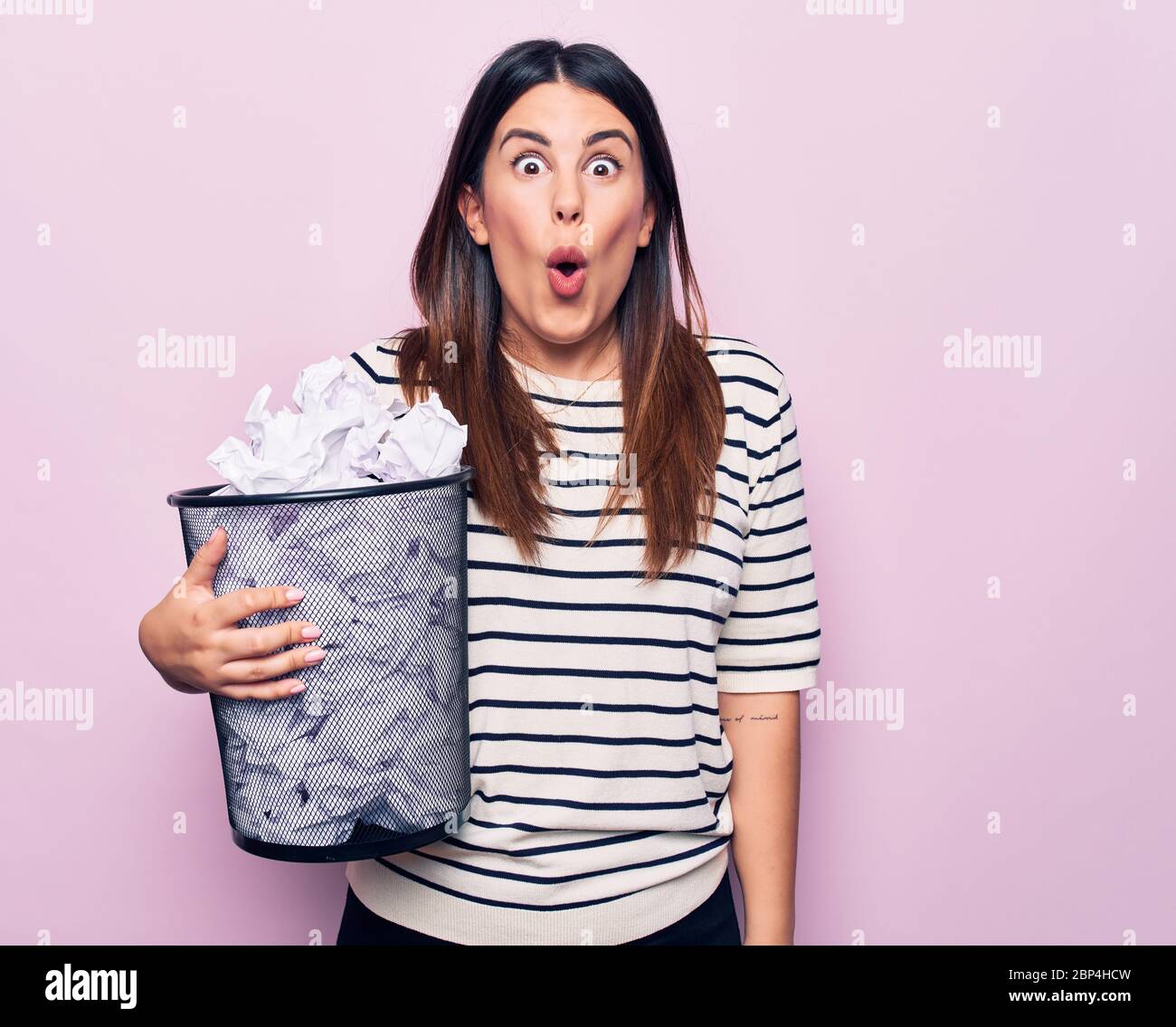 Young beautiful brunette woman holding full paper bin of crumpled ...