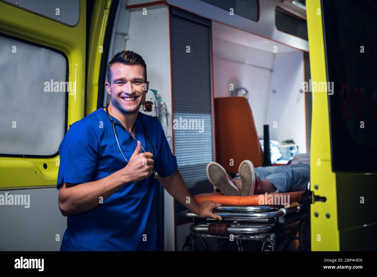 A young paramedic in a blue uniform taking away his patient by an ...