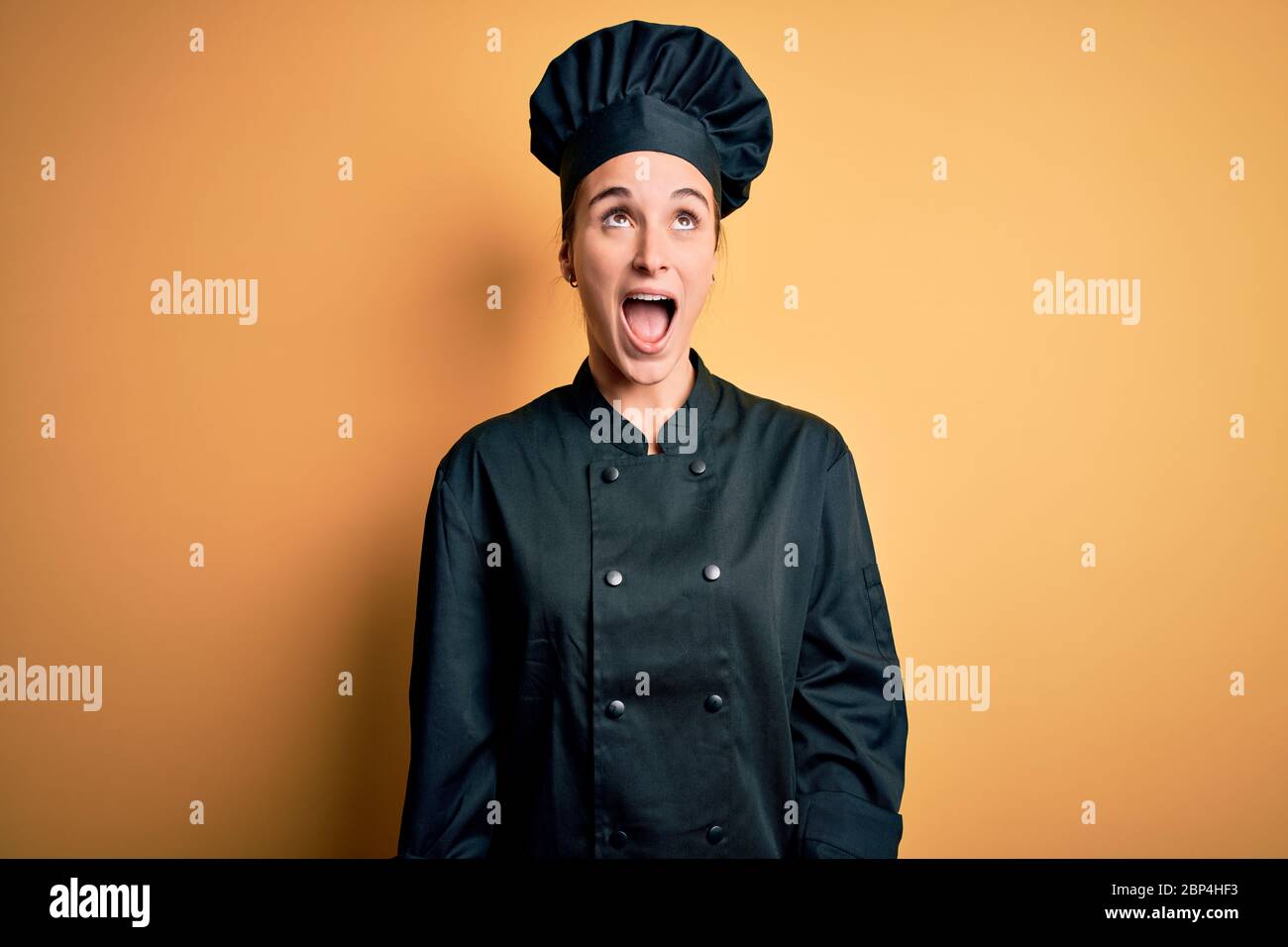 Young beautiful chef woman wearing cooker uniform and hat standing over ...