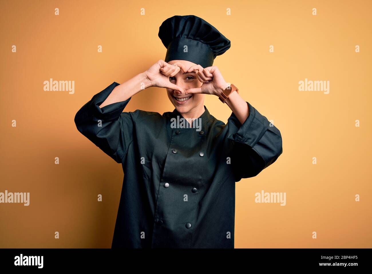 Young beautiful chef woman wearing cooker uniform and hat standing over ...