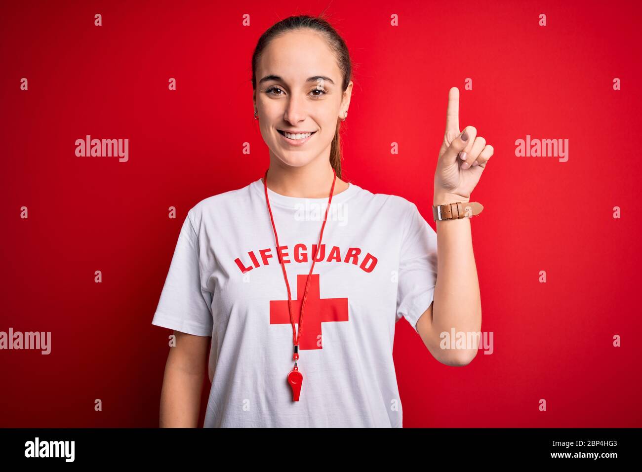 Beautiful lifeguard woman wearing t-shirt with red cross using whistle ...