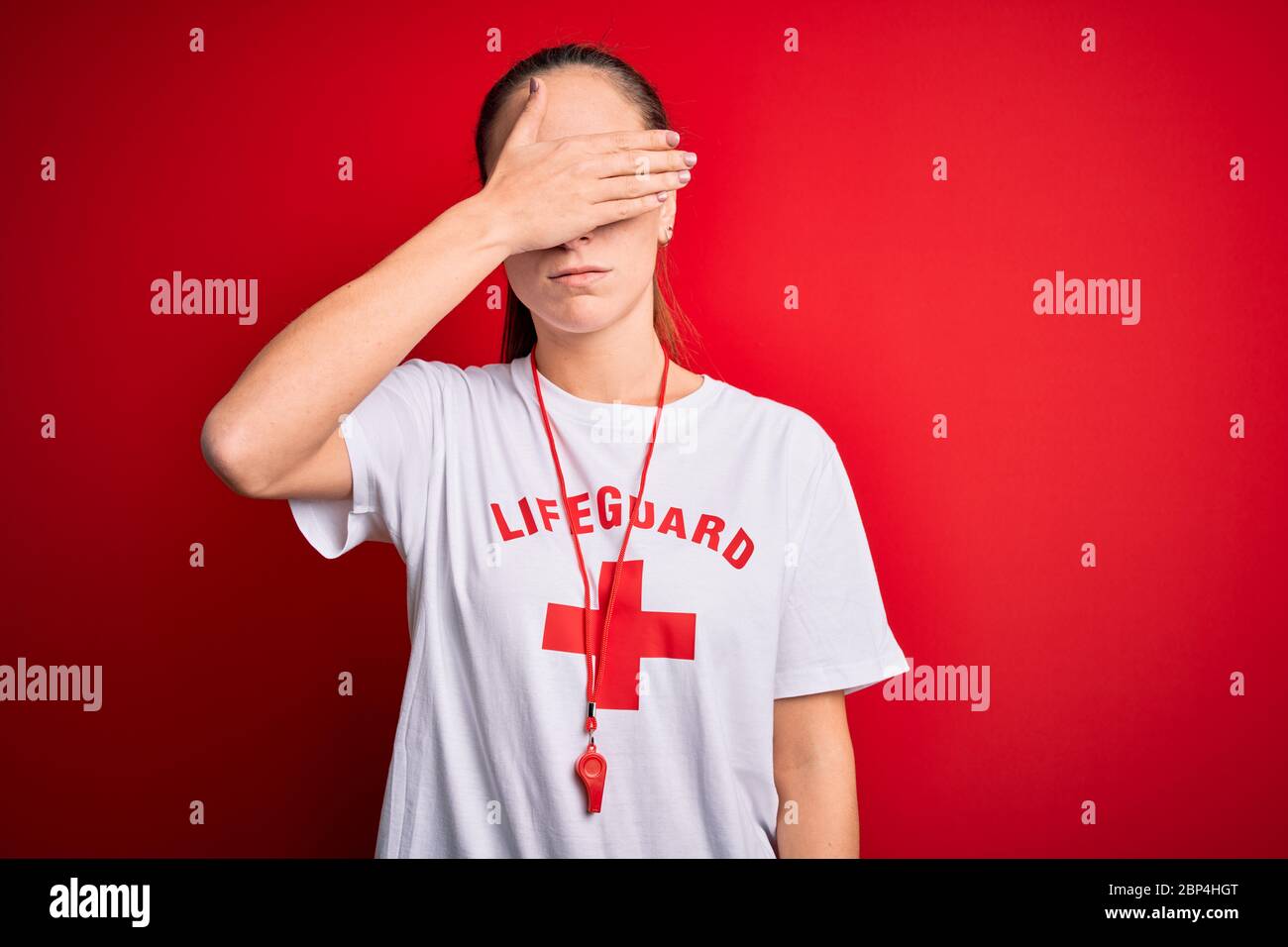Beautiful lifeguard woman wearing t-shirt with red cross using whistle ...