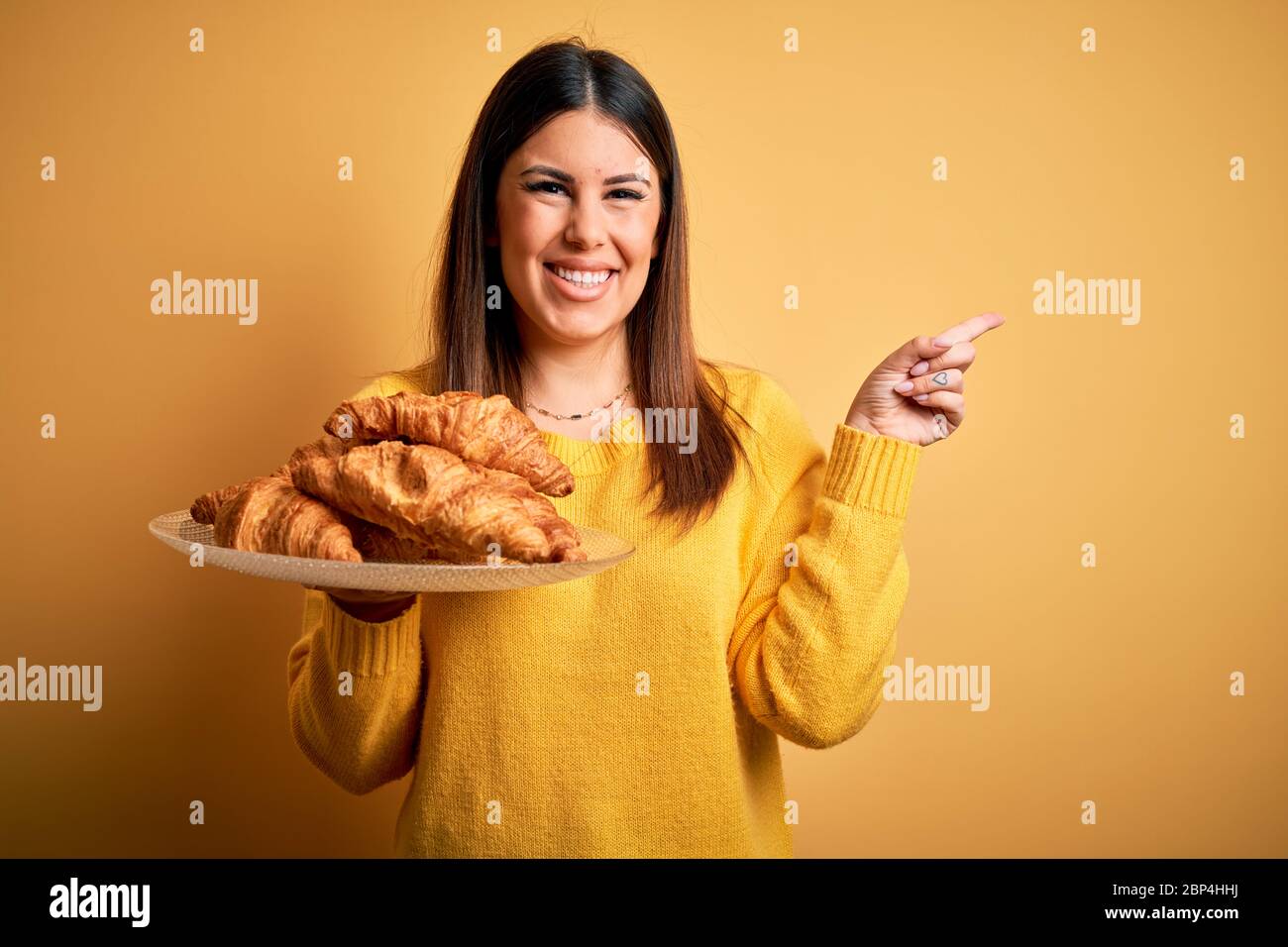 Young beautiful woman holding french croissant pastry over yellow ...