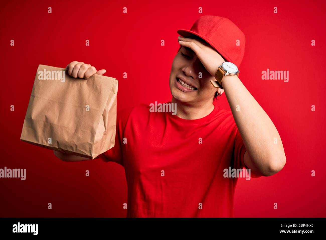 Young handsome chinese delivery man holding takeaway paper bag with ...