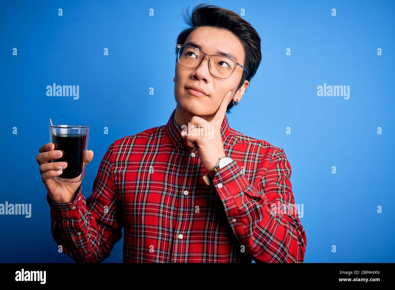Young handsome chinese man drinking glass of coffee over isolated blue ...