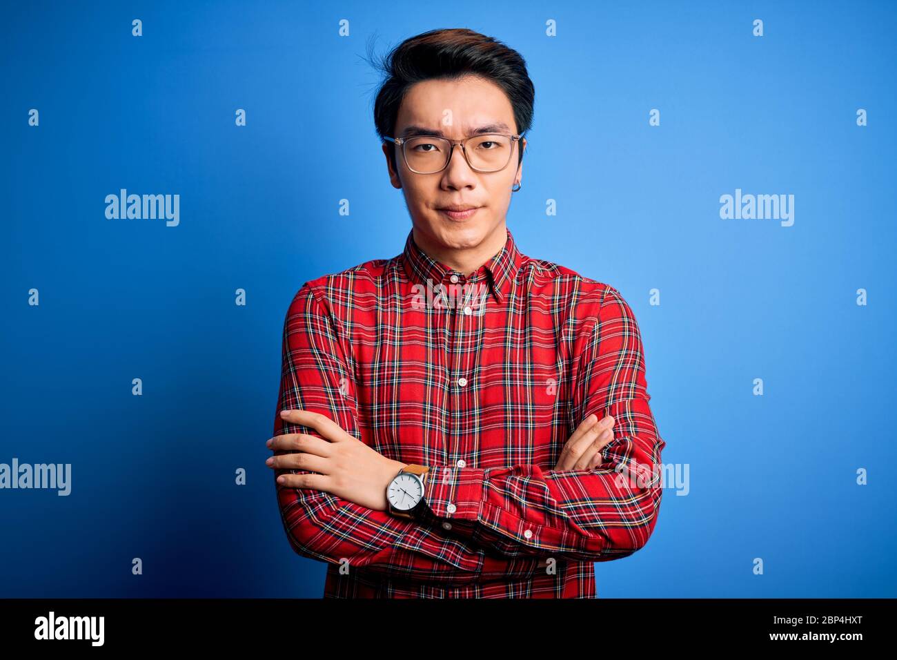 Young handsome chinese man wearing casual shirt and glasses over blue ...