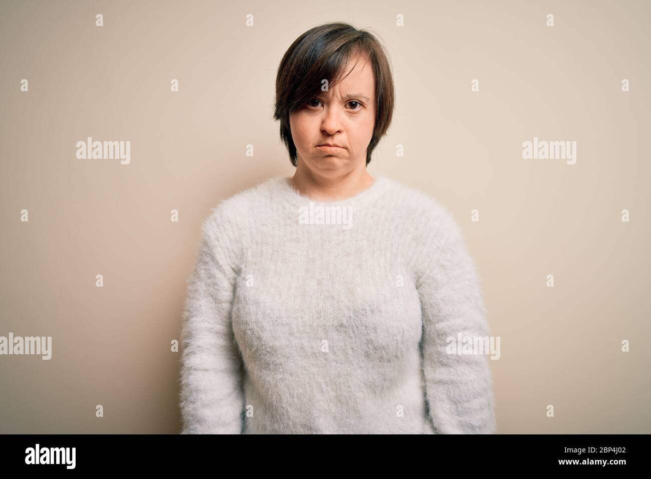 Young down syndrome woman standing over isolated background depressed ...