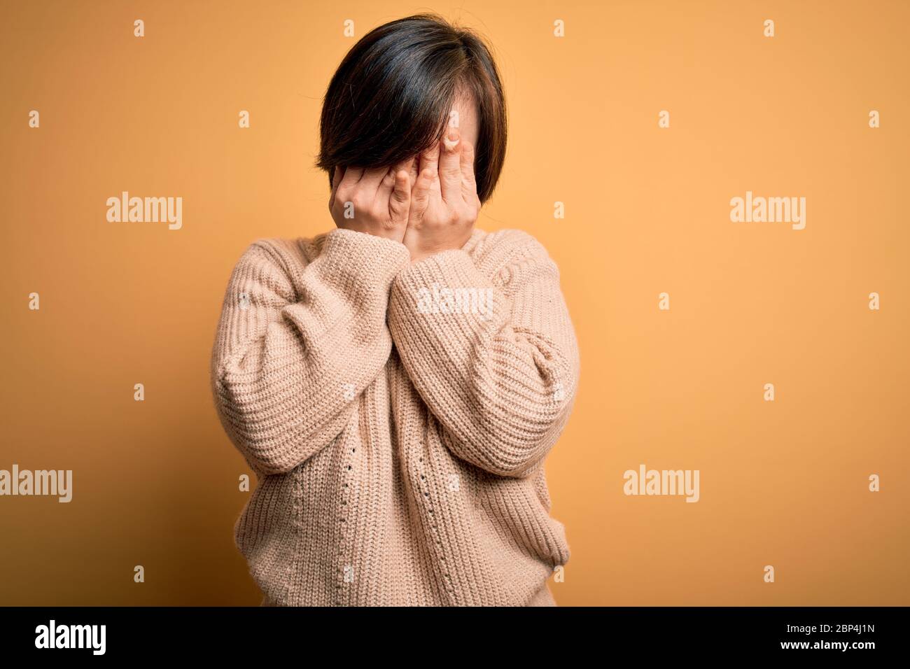Young down syndrome woman wearing casual sweater over yellow background ...