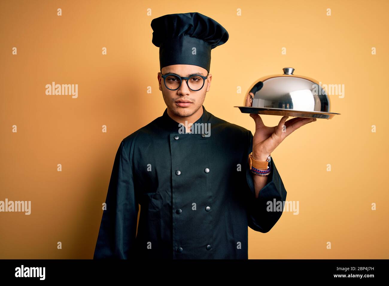 Young brazilian chef man wearing cooker uniform and hat holding tray ...