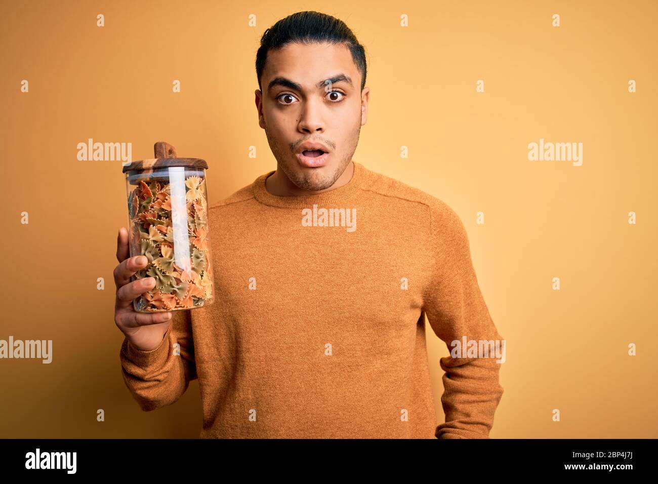 Young brazilian man holding jar with Italian dry pasta over isolated ...