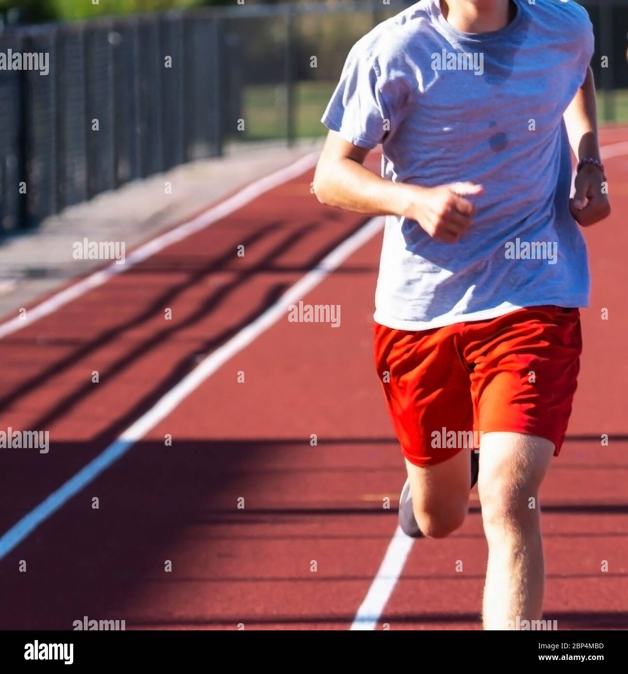 Front view of a high school runner running on a red track in his lane ...