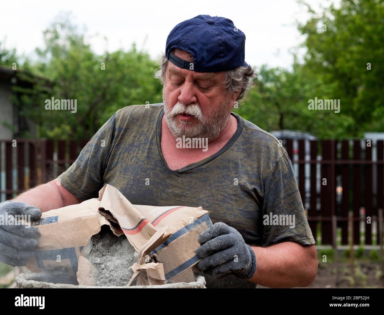 Mature Caucasian man pours cement from a bag into a concrete mixer ...