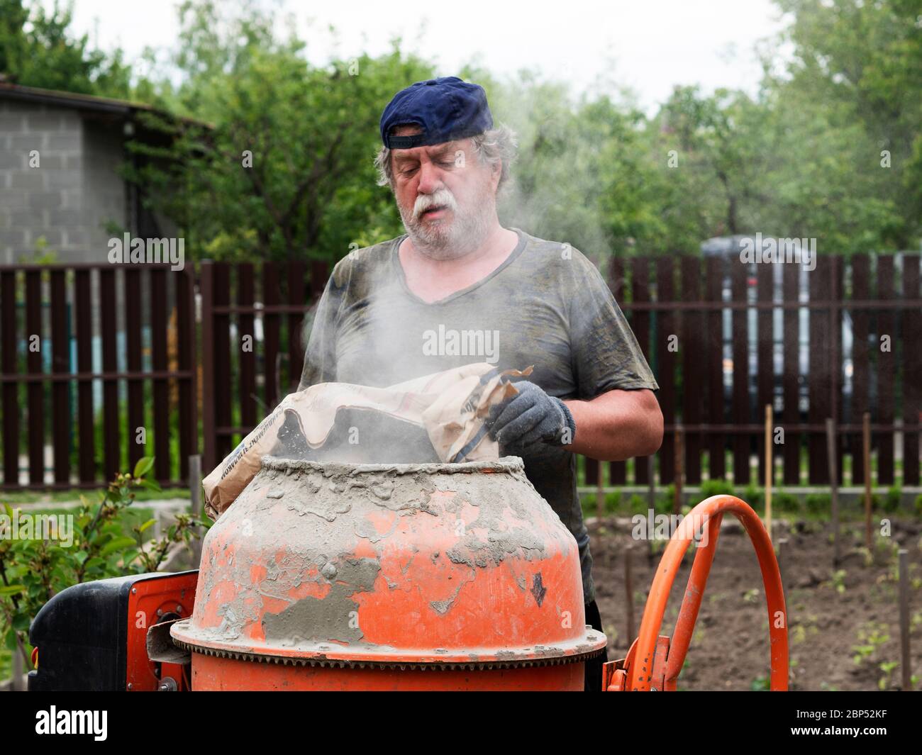 Mature Caucasian man pours cement from a bag into a concrete mixer ...