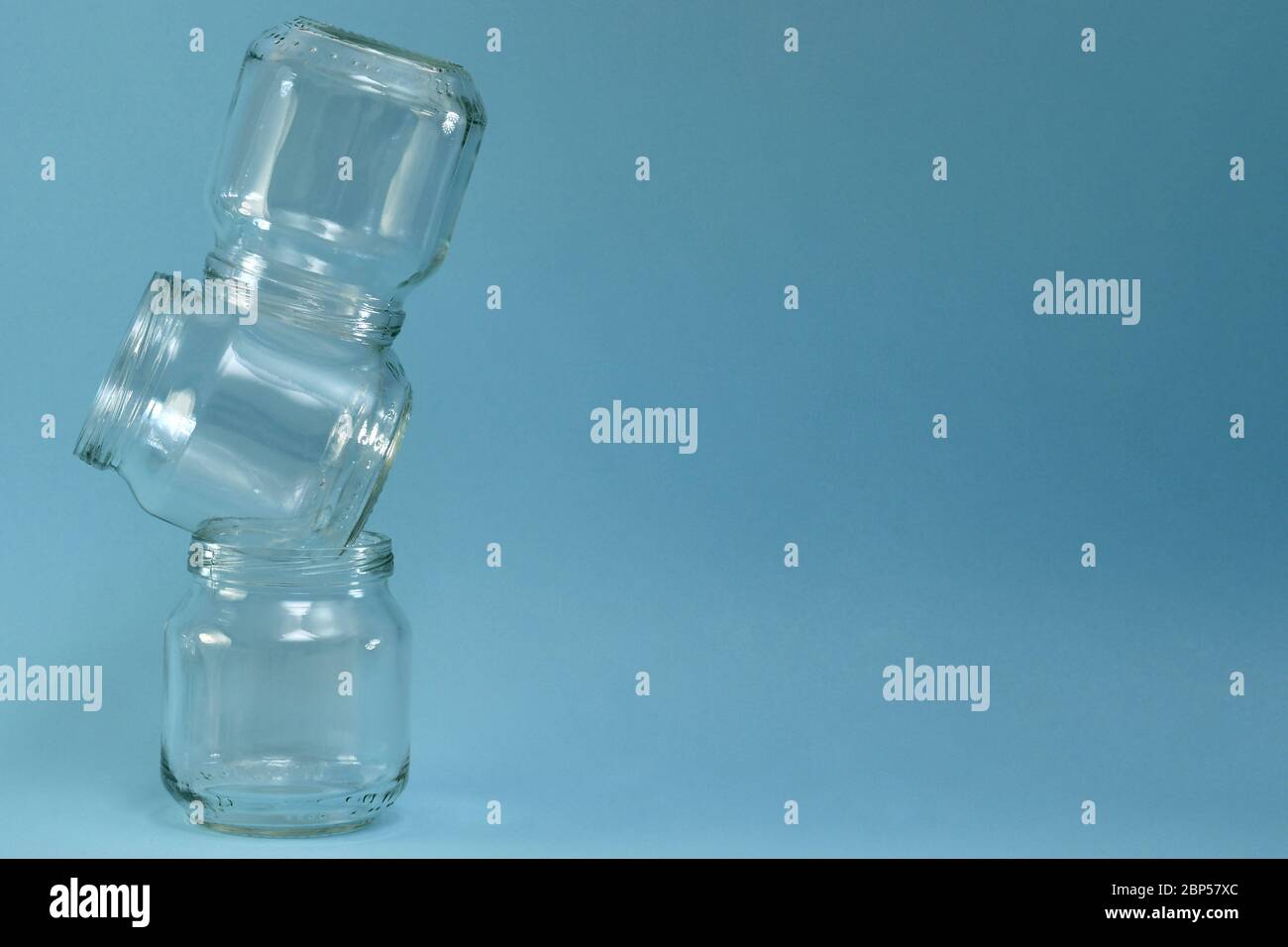 Vertical row of crooked glass jars on top of each other on a blue ...