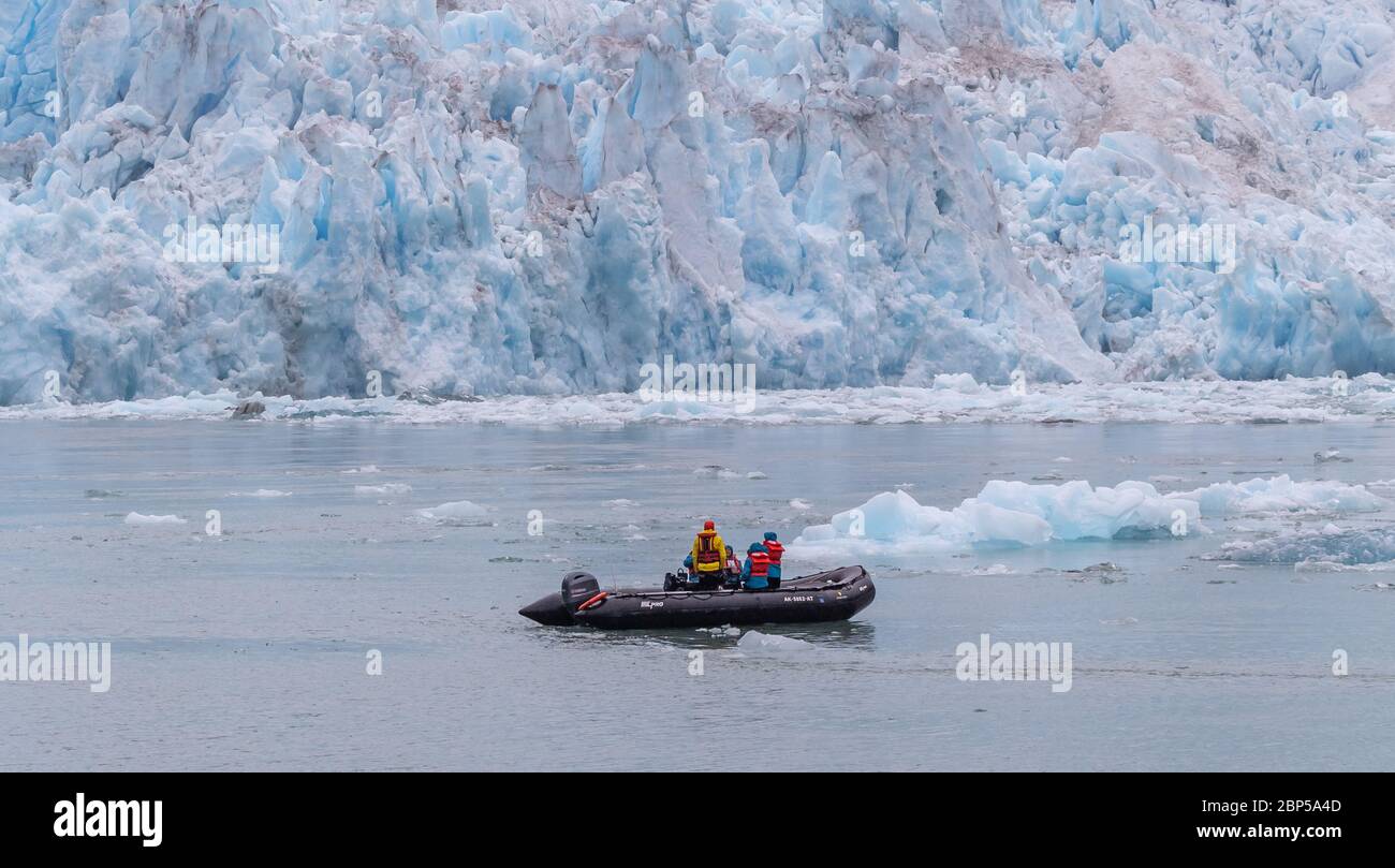 Tourists and a guide in a speedboat drifting among icebergs and a ...