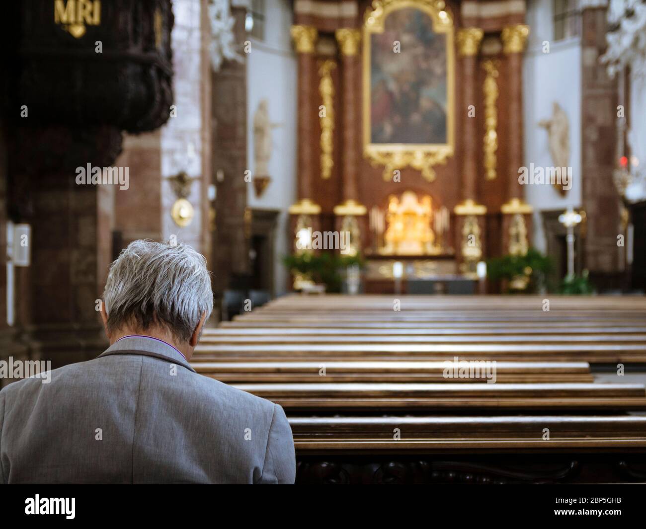 Rear view of an elderly man sitting alone in church praying with the ...