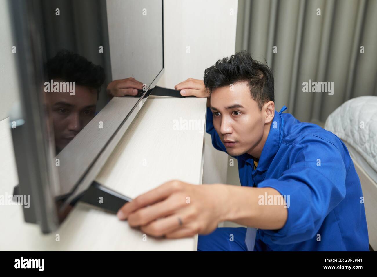 Serious service worker putting tv set on console in hotel room Stock ...