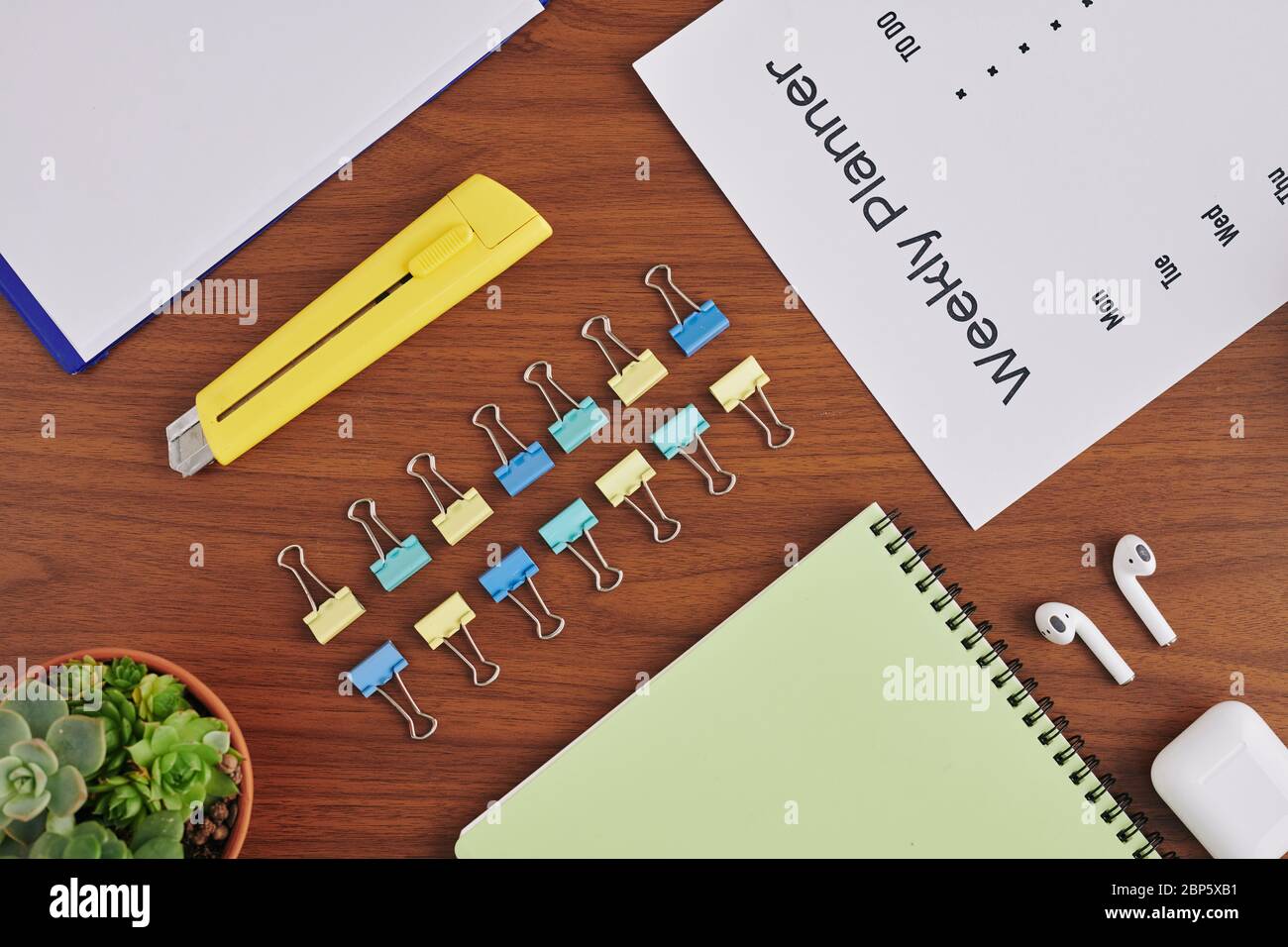 Weekly planner, colorful paper clips, paper knife and textbook on desk ...