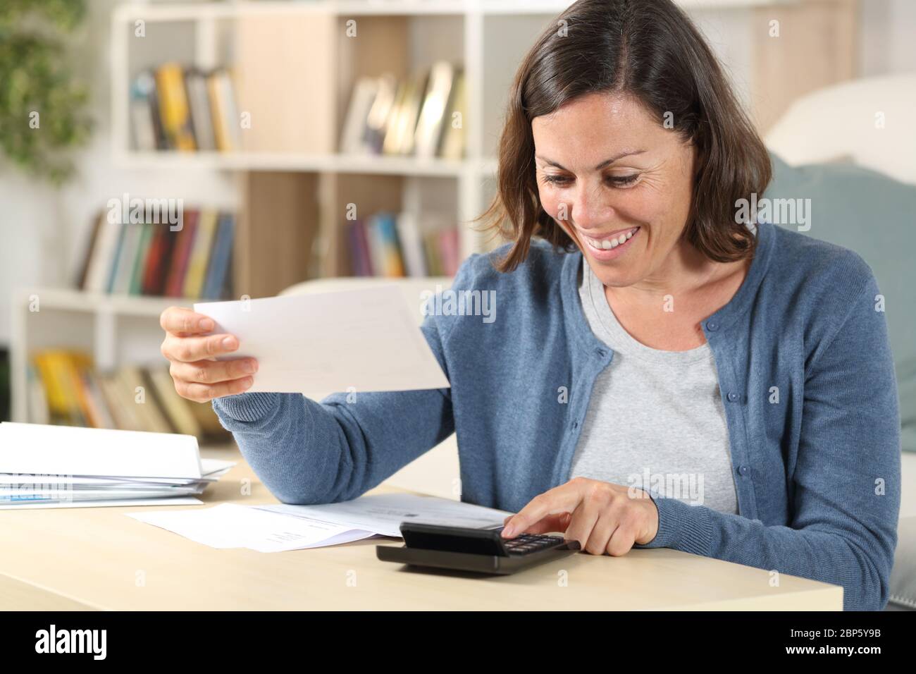 Happy adult woman calculating receipts with calculator sitting in the ...