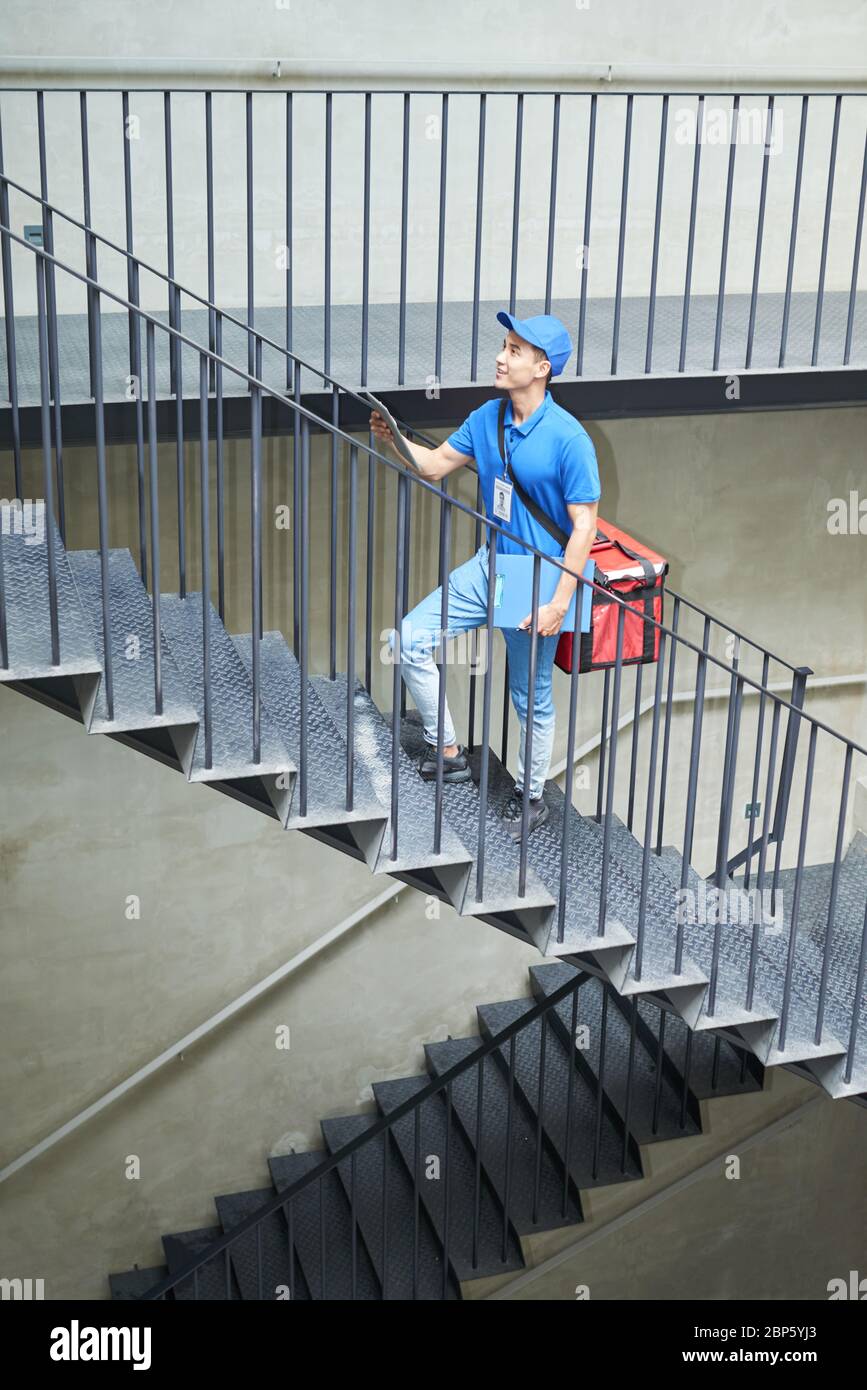 Smiling delivery man walking up the stairs with clipboard and portable ...