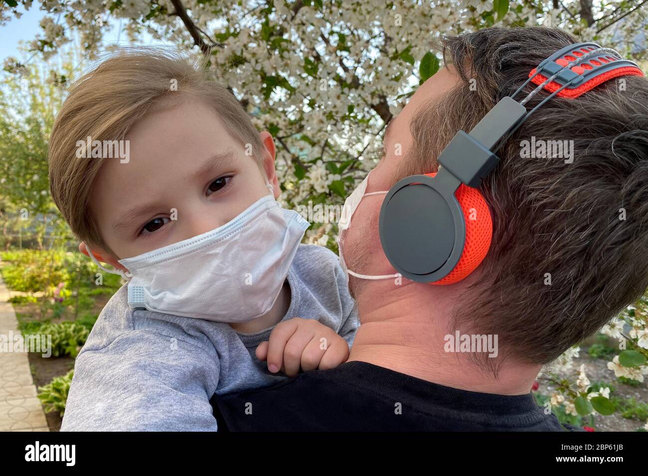 A little boy in medical mask hugs a man. Dad holds his son, they both ...
