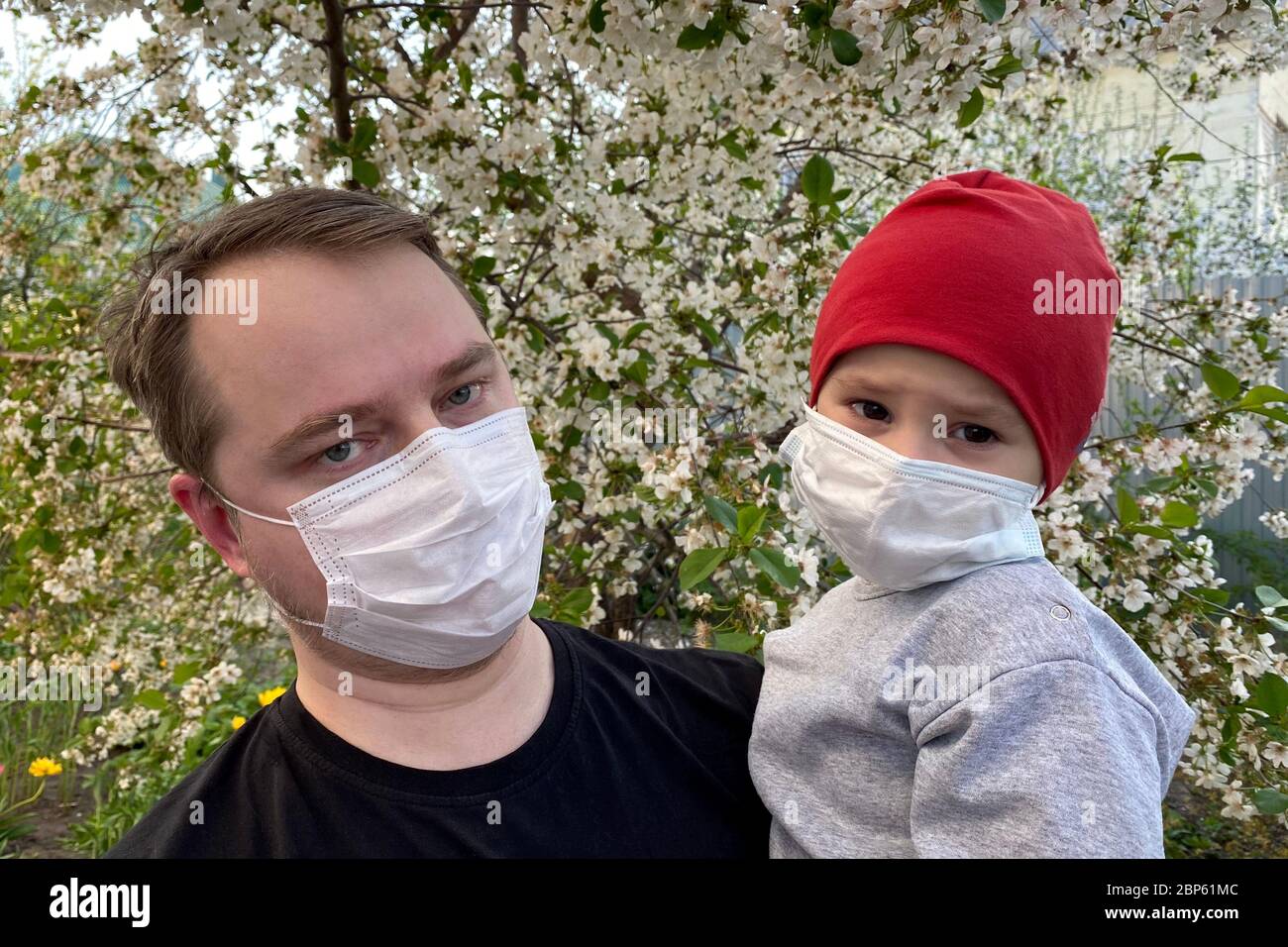 A little boy in medical mask hugs a man. Dad holds his son, they both ...