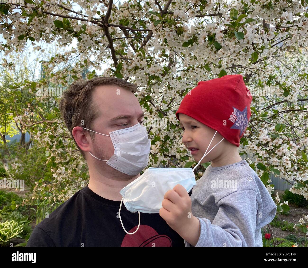 A little boy in medical mask hugs a man. Dad holds his son, they both ...