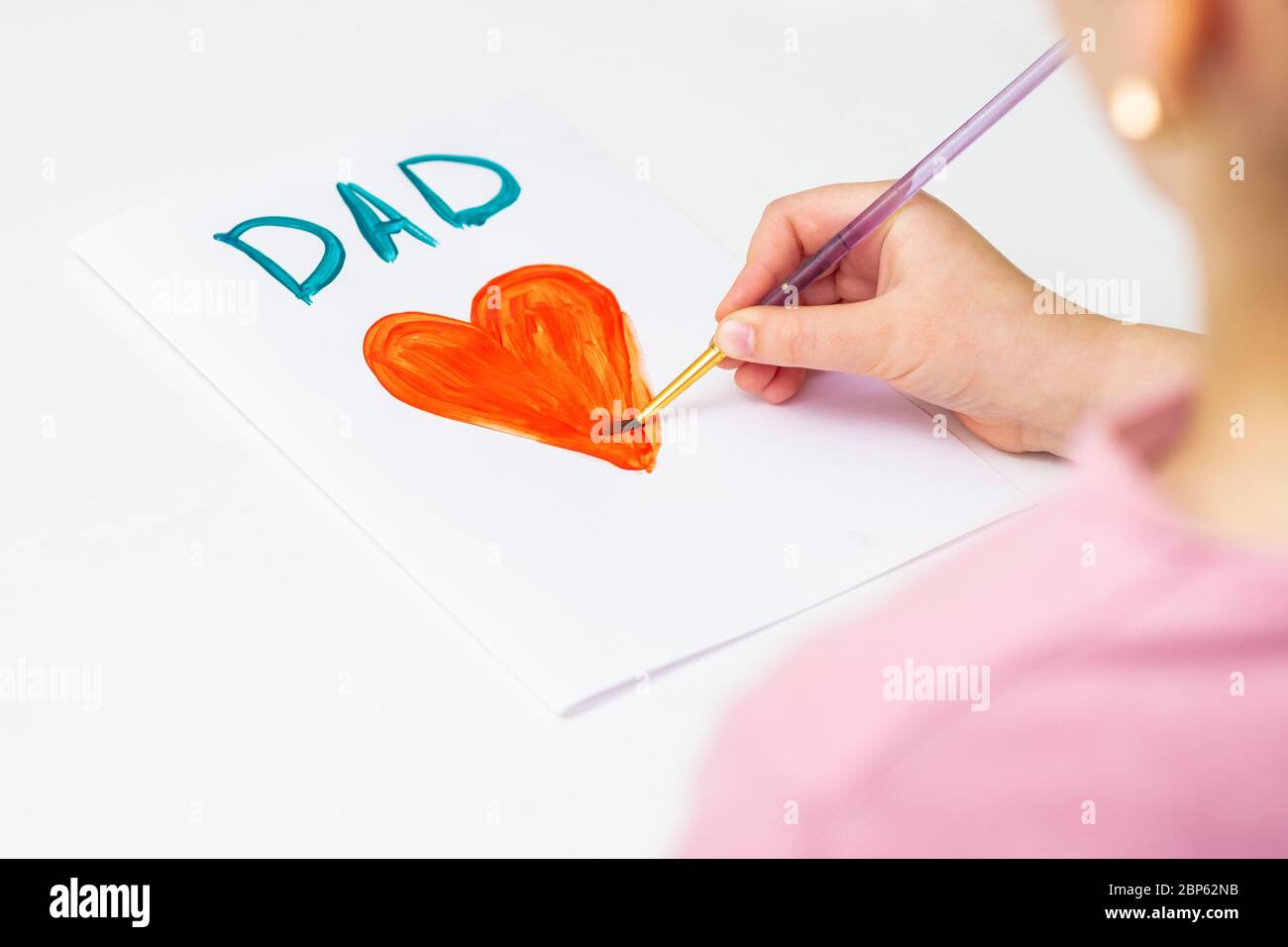 Back view of littel girl is drawing red heart with word Dad greeting ...