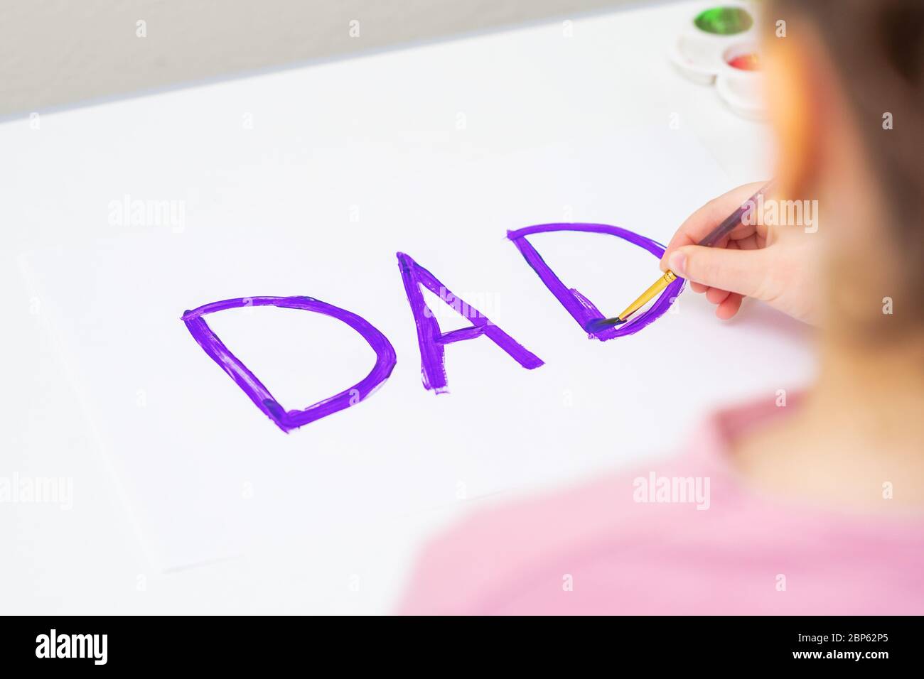 Hand of child drawing handwritten purple word Dad greeting card on ...