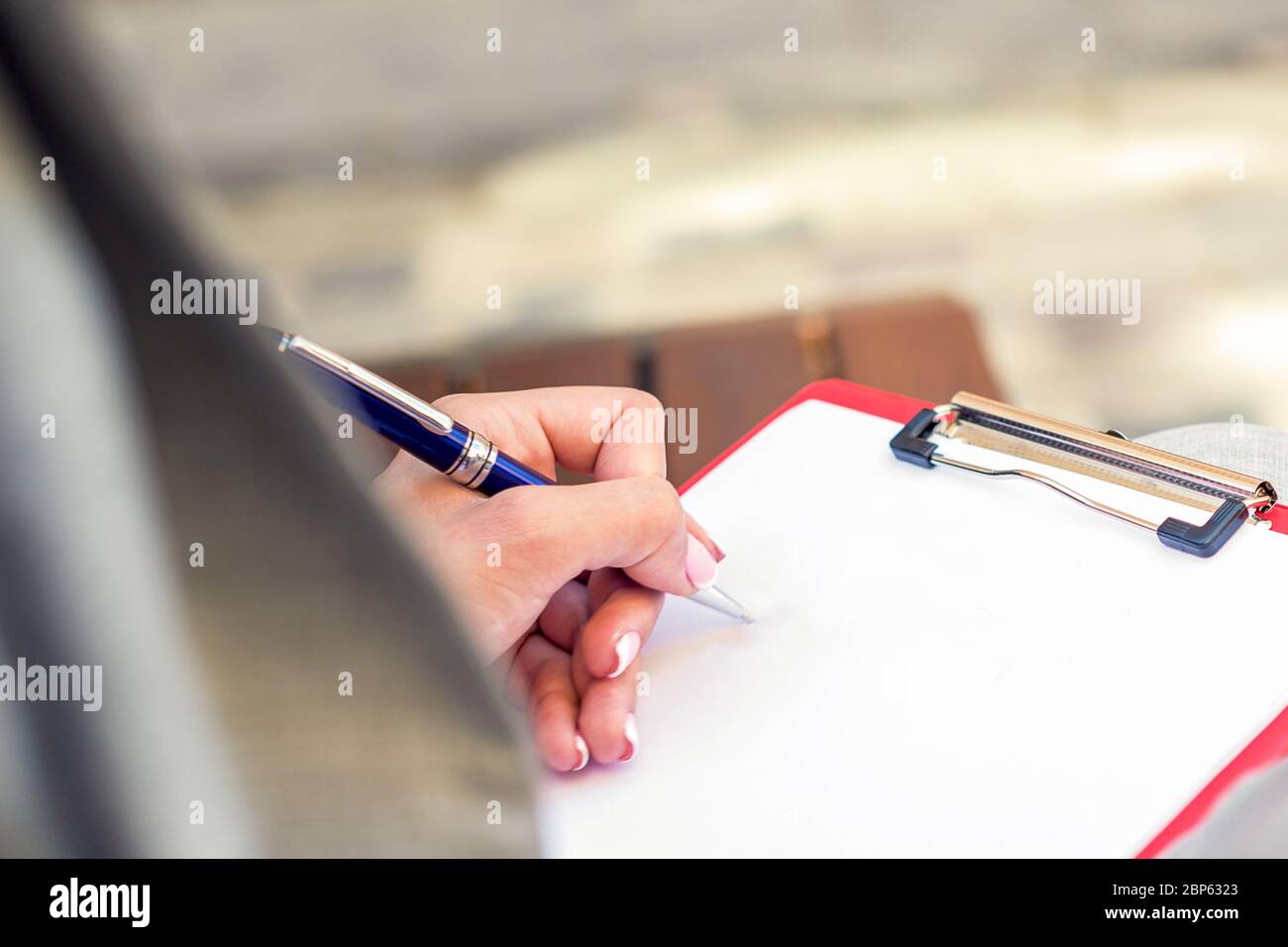 Close up of woman's left hand writing in a blank paper by pen outdoor ...