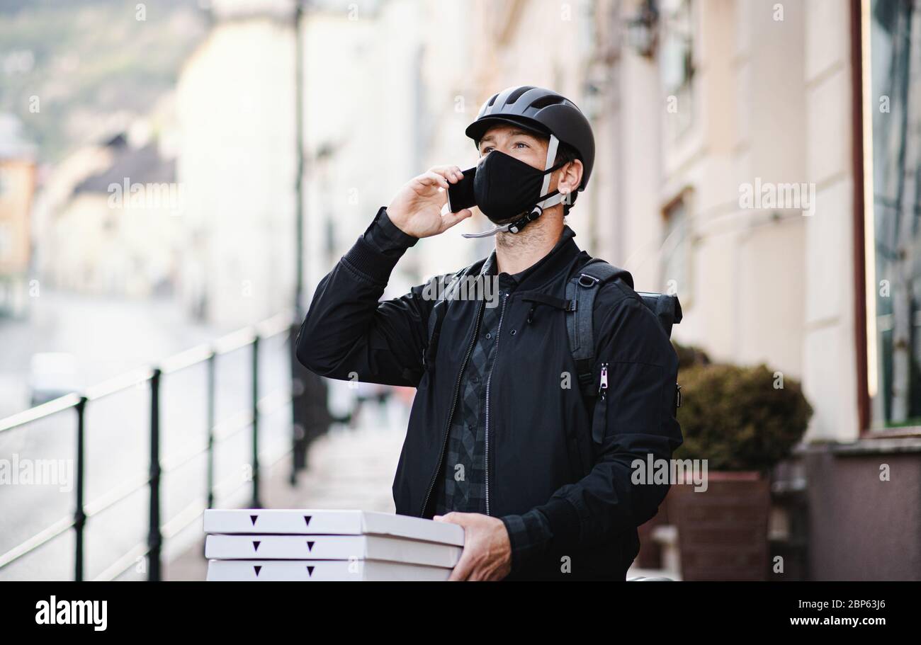 Delivery man courier with face mask and smartphone delivering pizza in ...