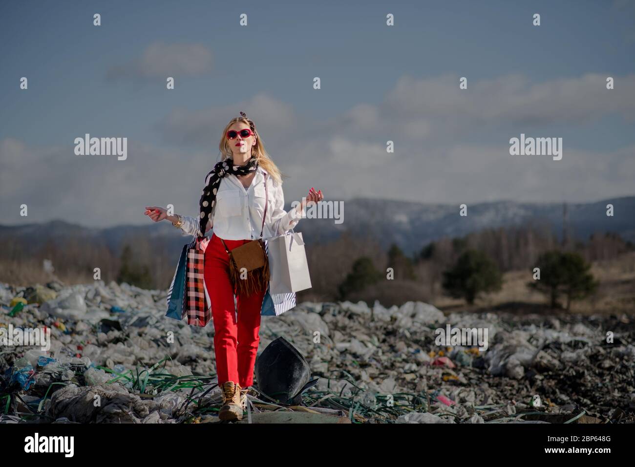 Woman with shopping bags on landfill, consumerism versus pollution ...