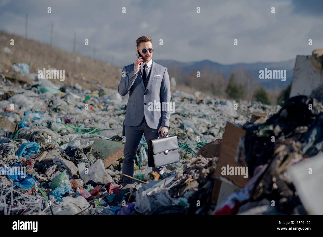 Businessman with smartphone on landfill, consumerism versus pollution ...