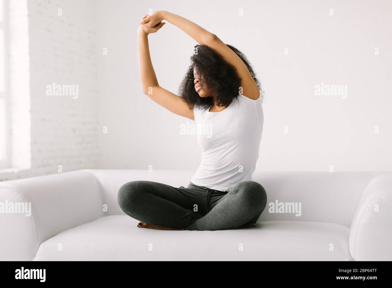 An African American young women sitting in the lotus position on white ...